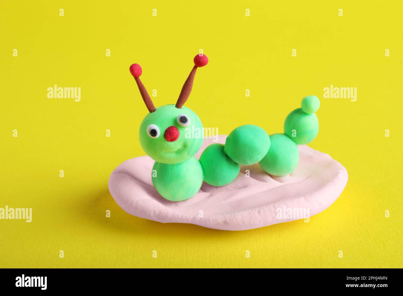 Colorful caterpillar made from play dough on yellow background, closeup ...
