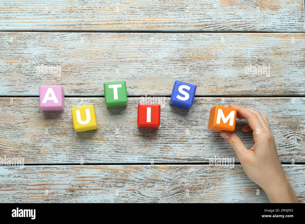 Woman making word Autism with colorful cubes on light wooden table, top ...