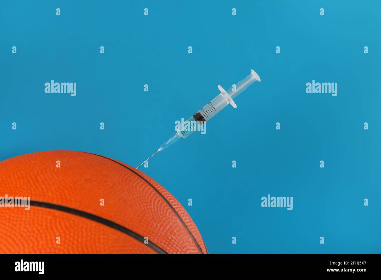 Closeup view of basketball ball with syringe on light blue background ...