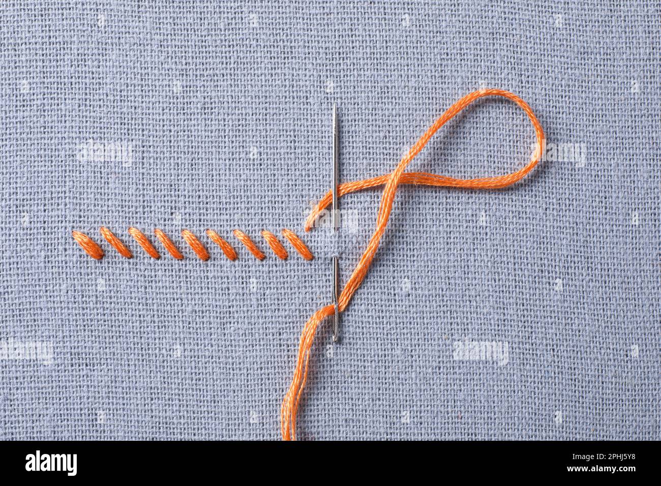 Needle with orange embroidery floss and row of stitches on grey fabric ...