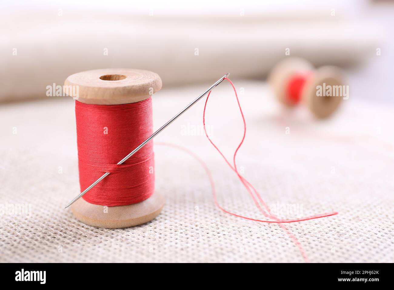 Spool of red sewing thread with needle on white fabric, closeup Stock ...
