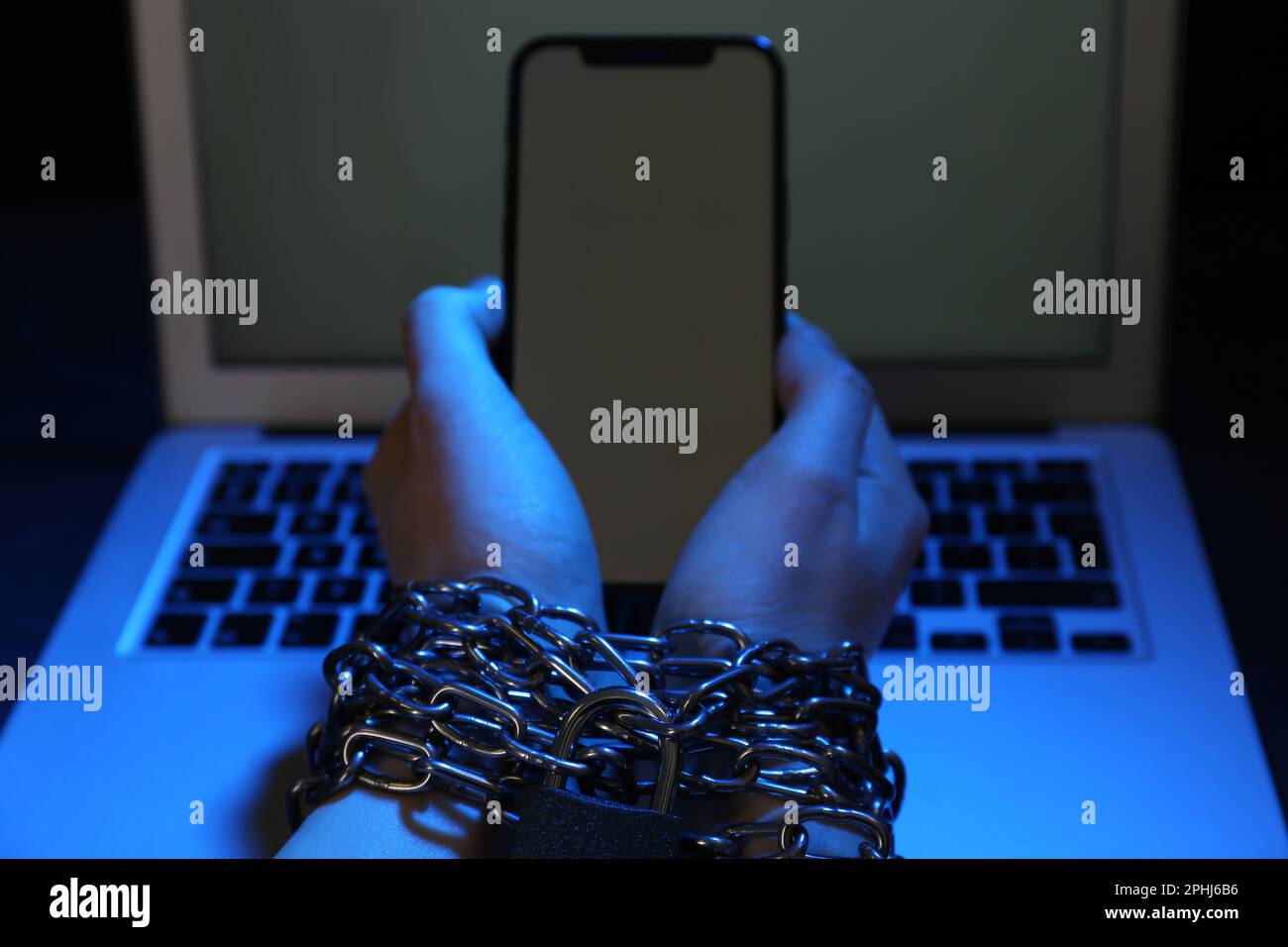 Woman with chained hands holding smartphone near laptop on dark ...