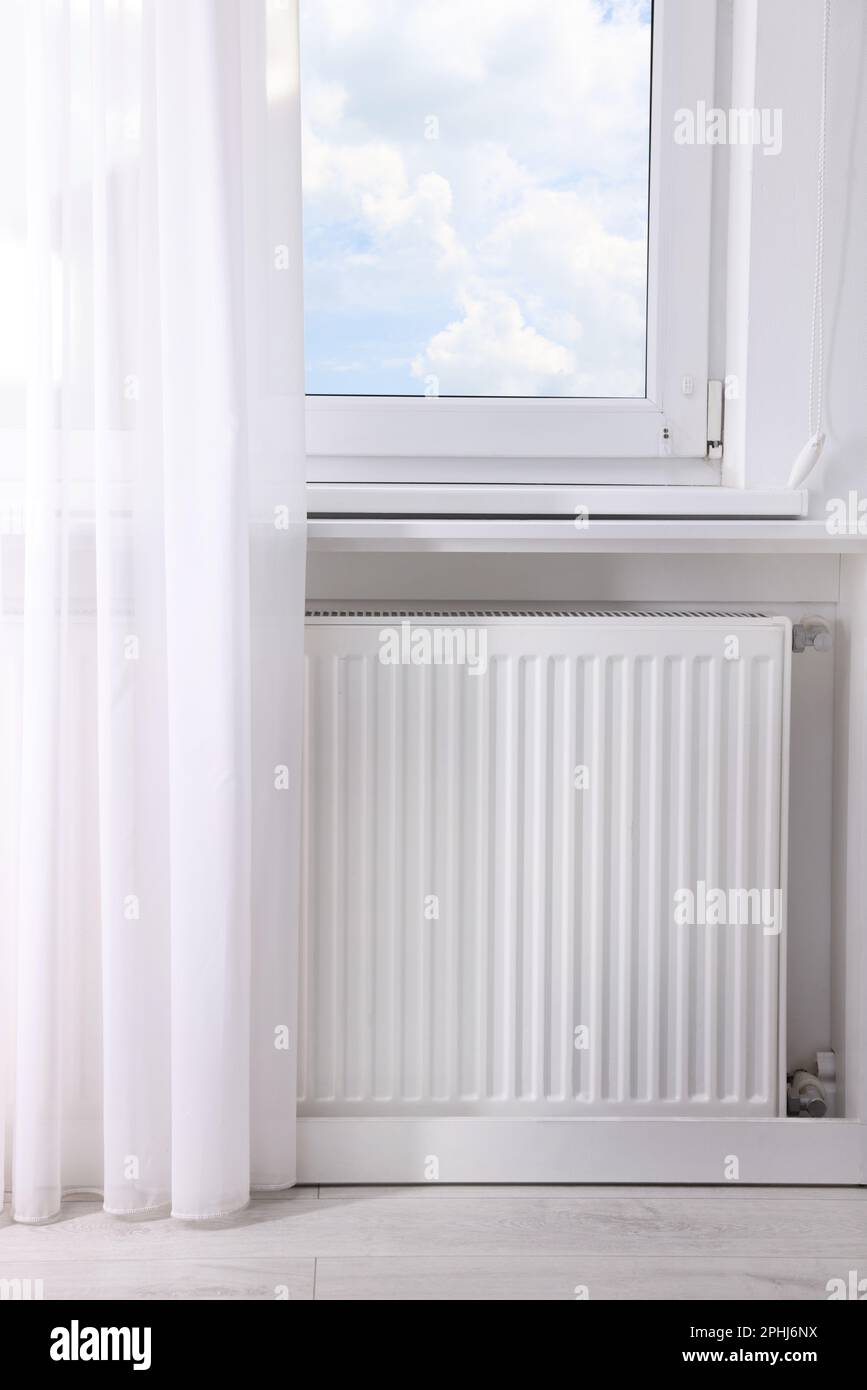 Modern radiator on wall under window indoors. Central heating system ...