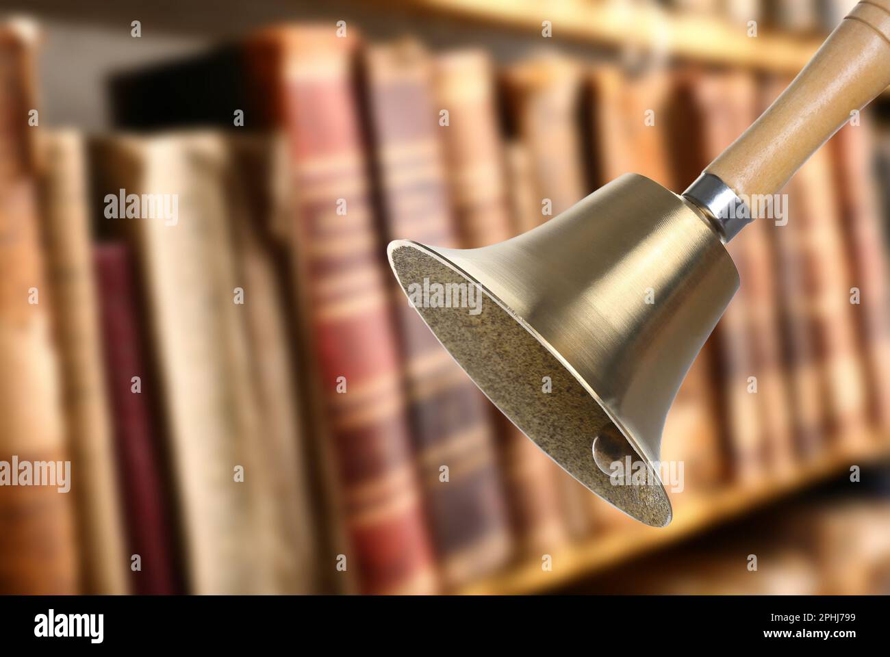 Golden school bell with wooden handle and blurred view of books on ...