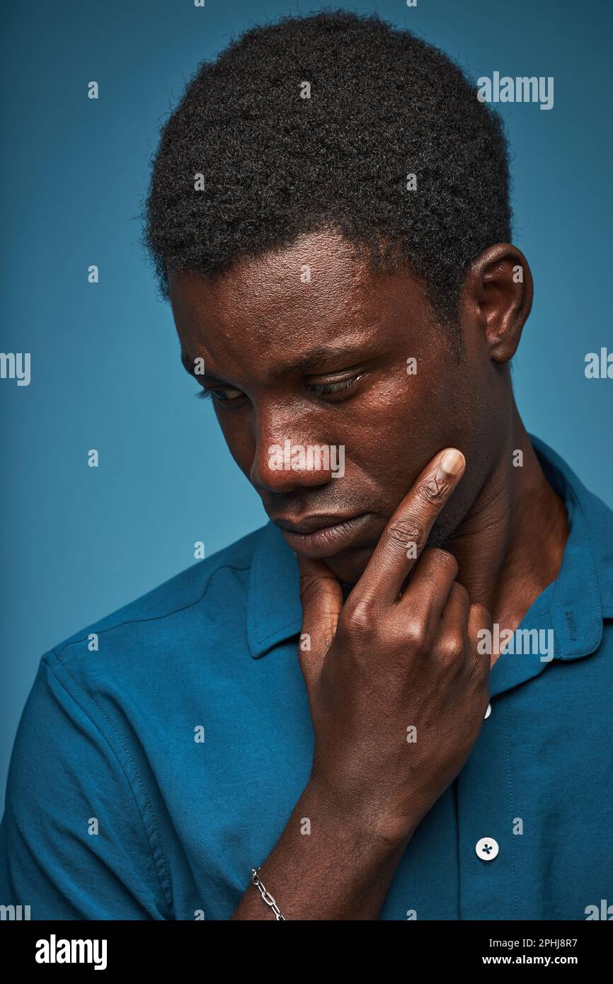 Vertical closeup portrait of young black man thinking against blue ...