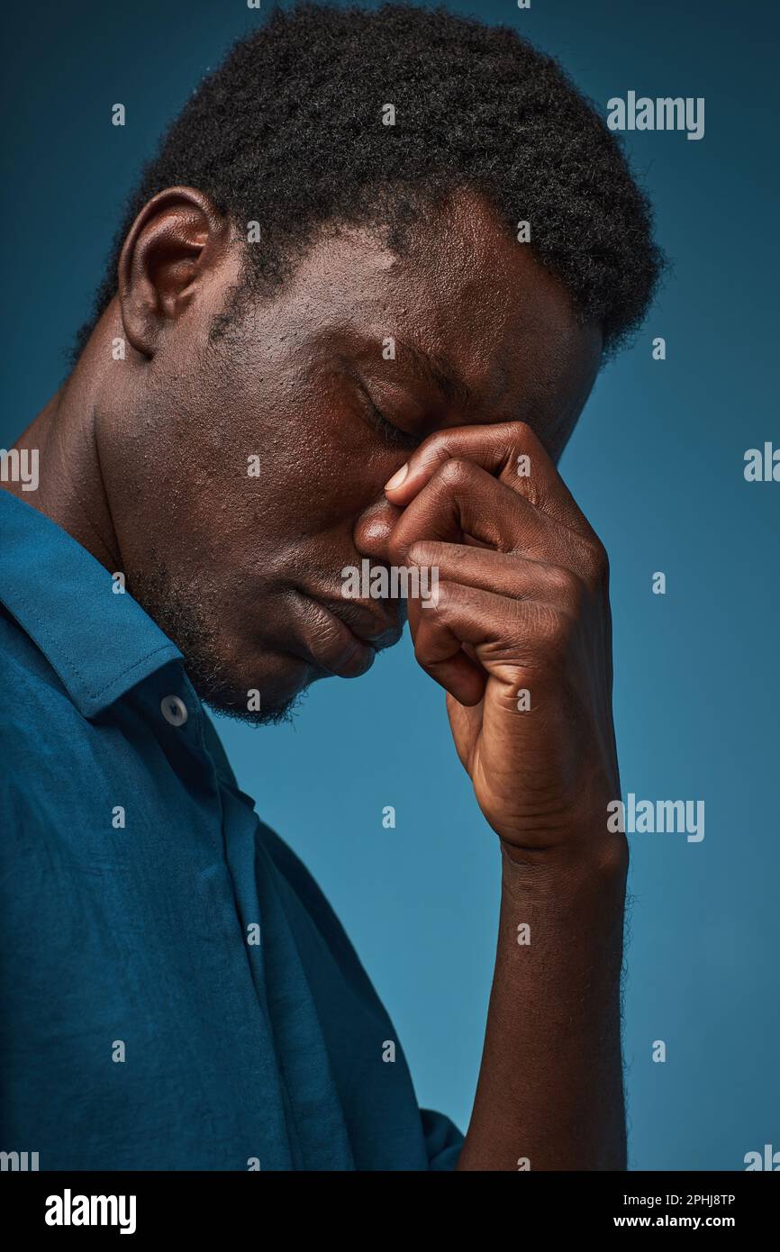 Side view portrait of stressed black man with eyes closed against blue ...