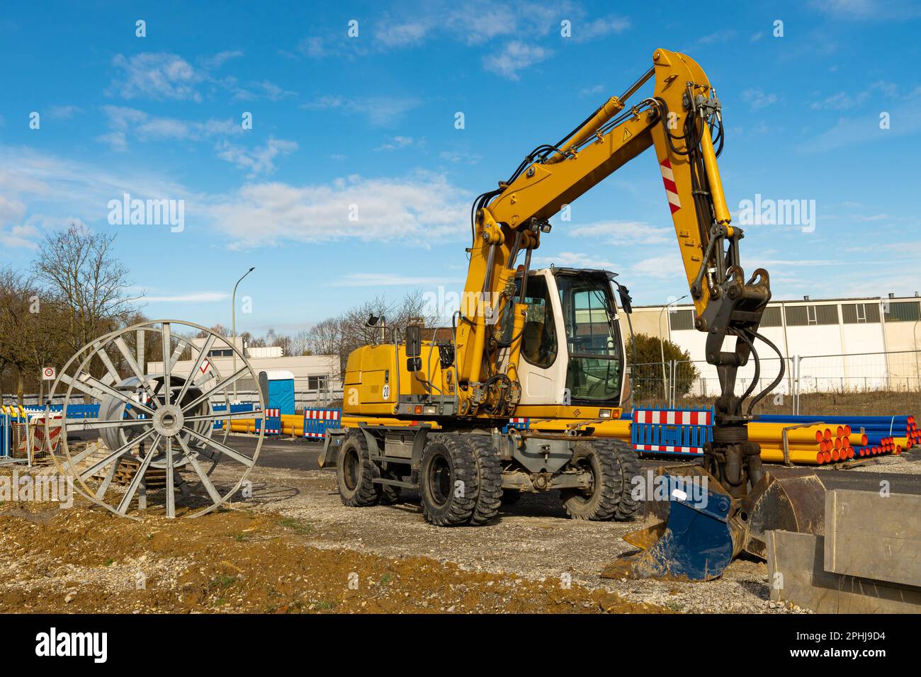 Yellow excavator at a construction site next to an empty cable drum ...