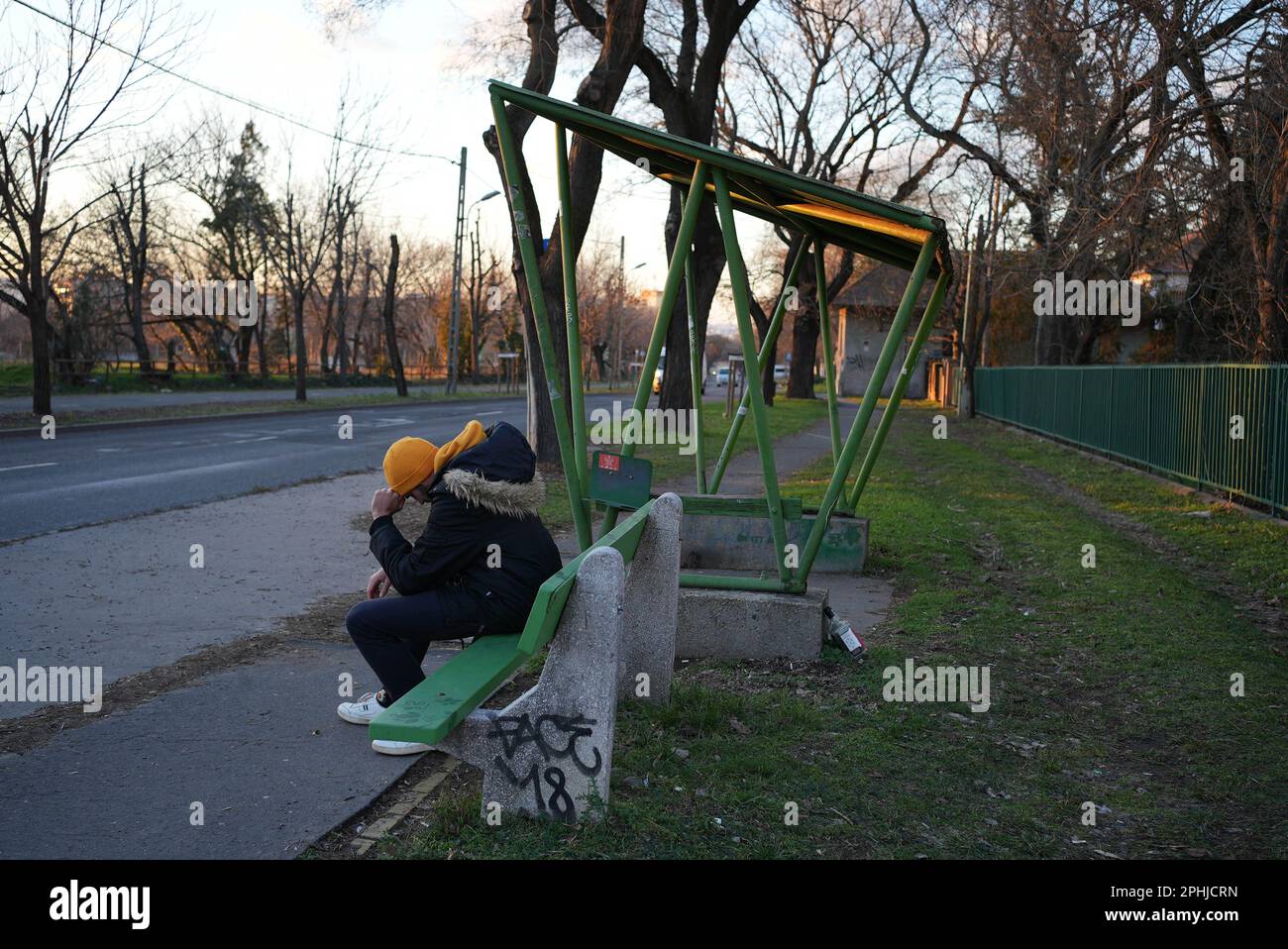 Young man sitting at a bus stop sad holding his head Stock Photo - Alamy