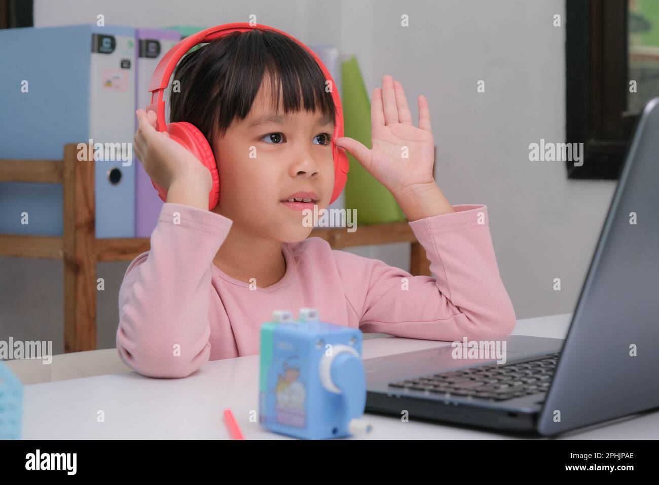 Cute elementary school girl wearing headphones and using a laptop ...