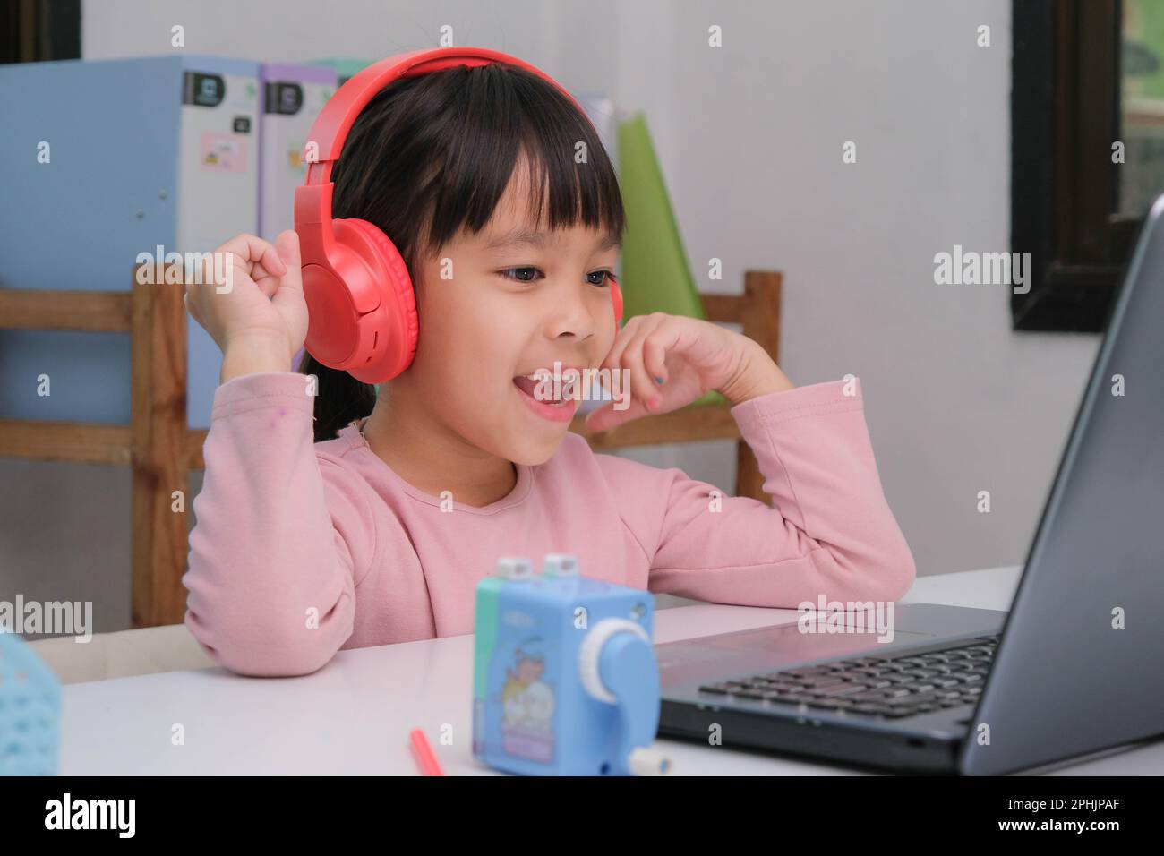 Cute elementary school girl wearing headphones and using a laptop ...