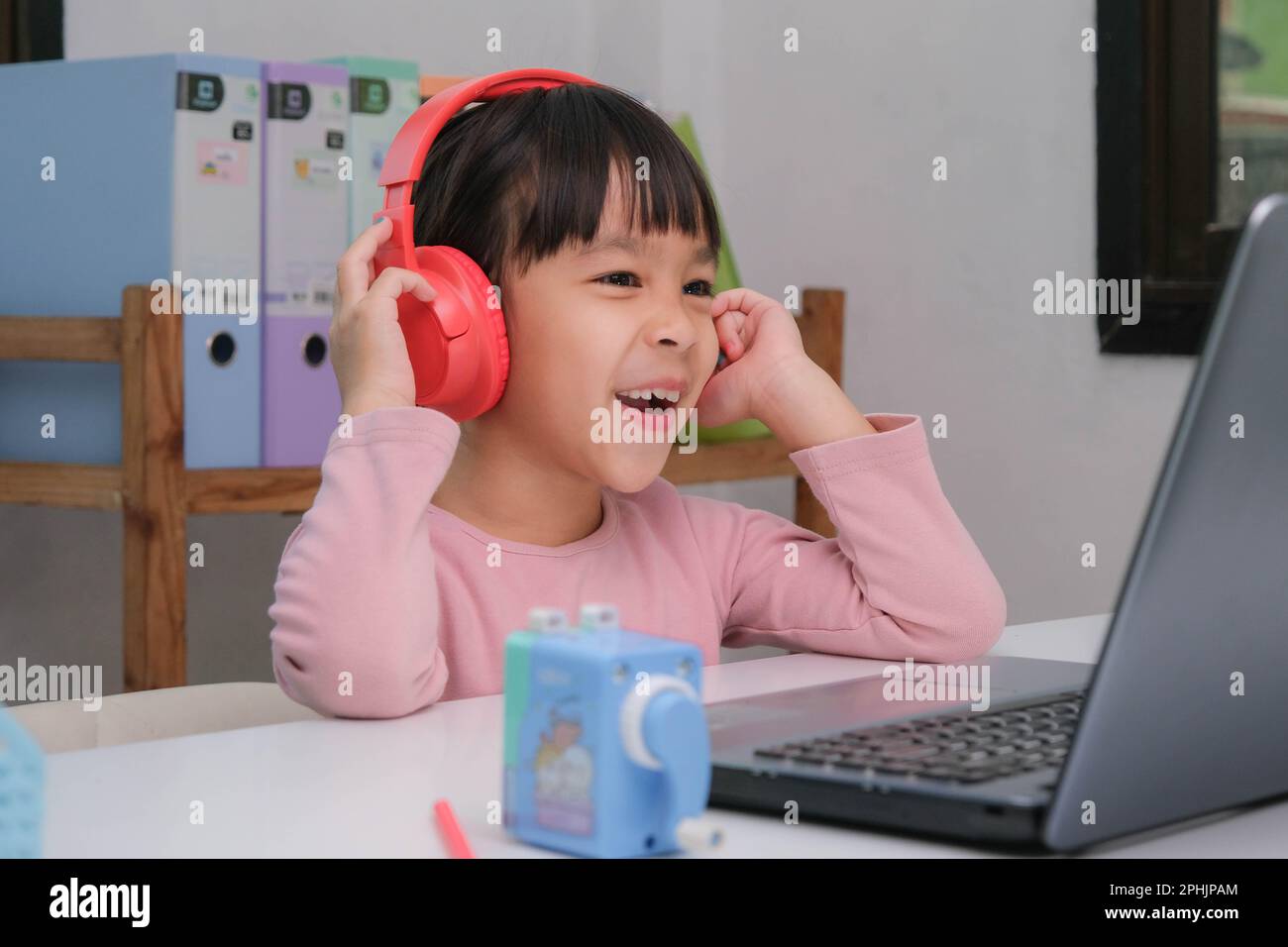 Cute elementary school girl wearing headphones and using a laptop ...