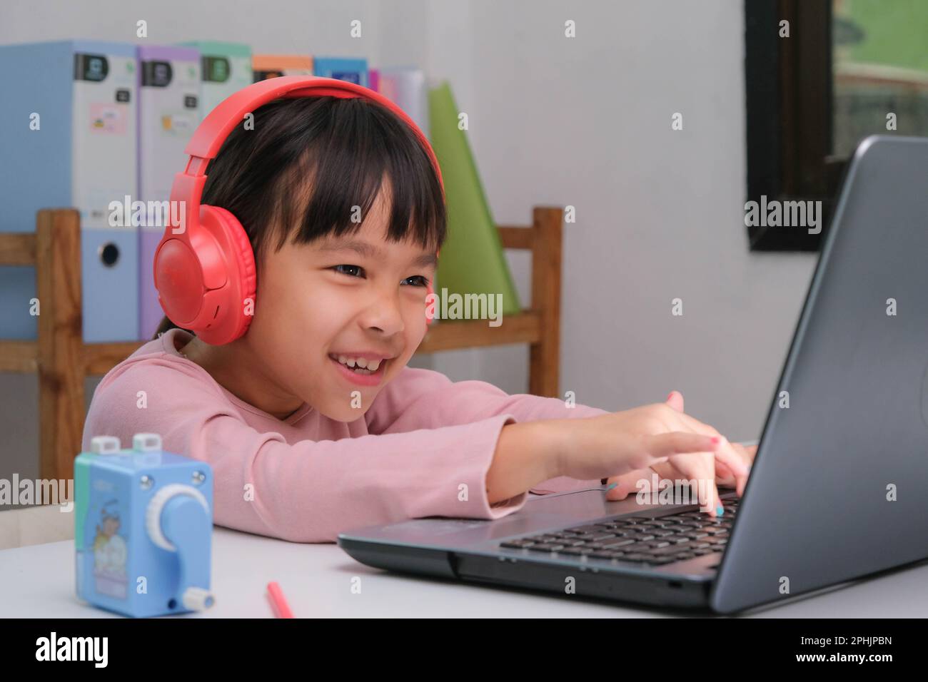 Cute elementary school girl wearing headphones and using a laptop ...