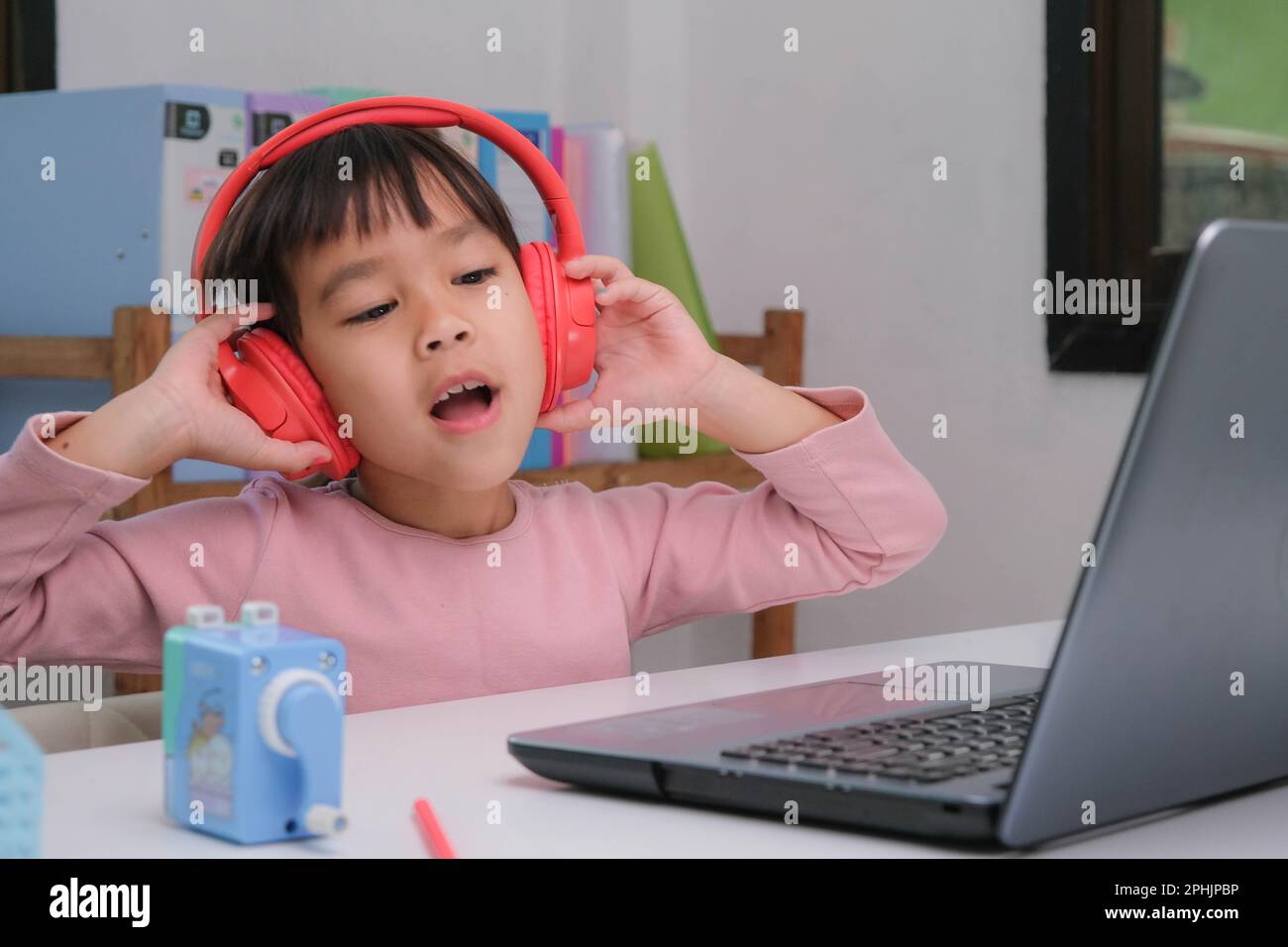 Cute elementary school girl wearing headphones and using a laptop ...