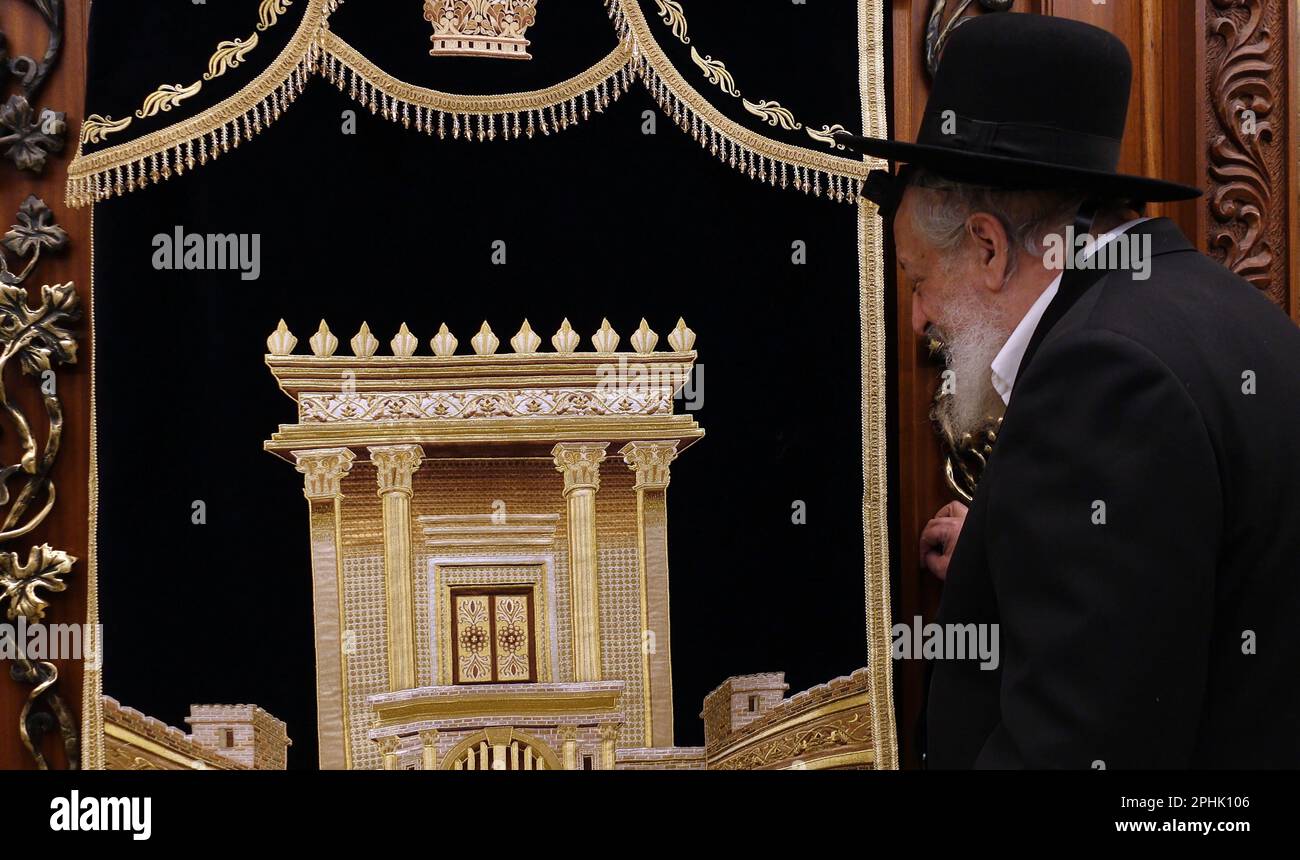 A haredi Jew prays next to a Torah Ark curtain decorated with a figure ...