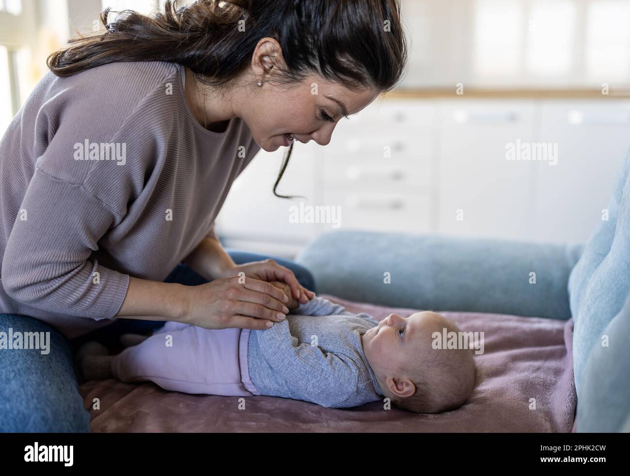 Cute newborn baby lying on back and smiling at mother on bed at home ...