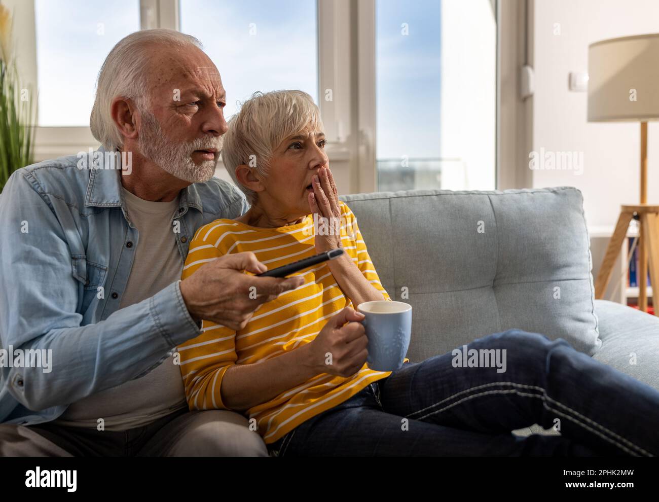 Senior couple watching scary scenes in movie on sofa at home. Mature ...