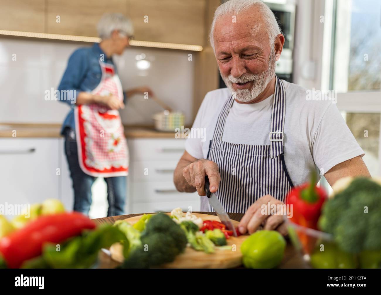 Senior couple preparing soup, husband cutting vegetable while wife ...
