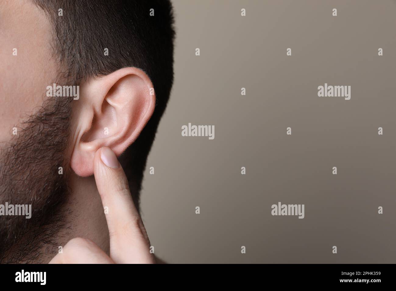 Man pointing at his ear on grey background, closeup. Space for text ...