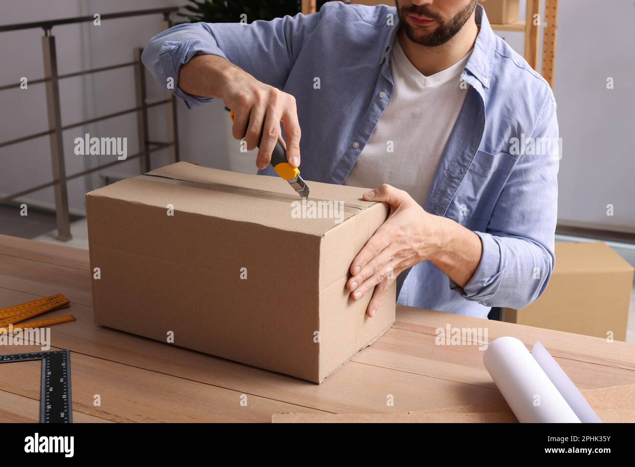 Man using utility knife to open parcel at wooden table indoors, closeup ...