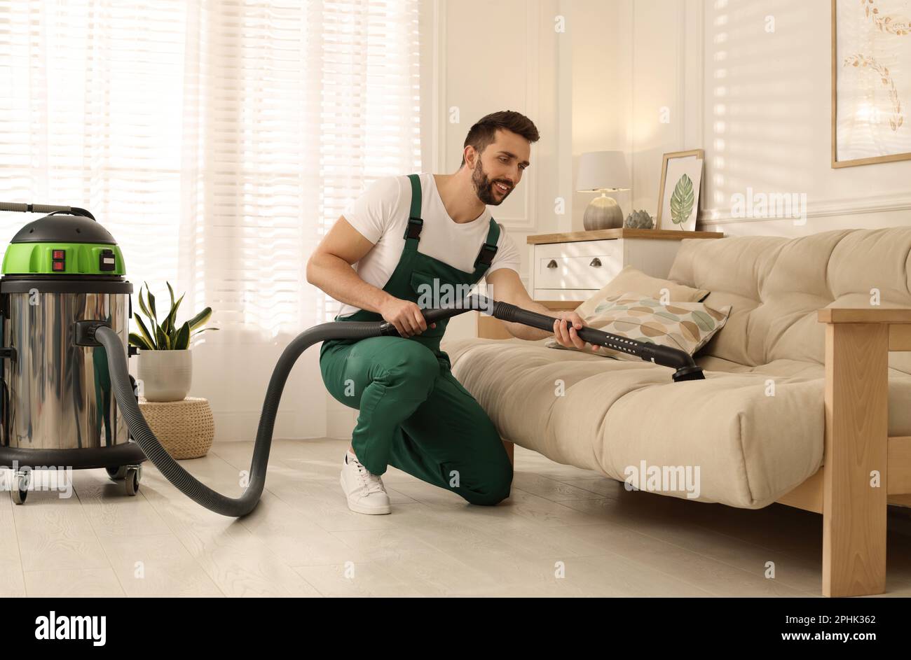Professional janitor vacuuming sofa in living room Stock Photo - Alamy