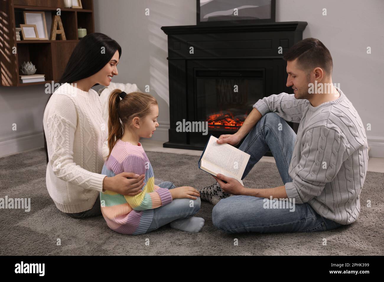 Happy family reading book together on floor near fireplace at home ...