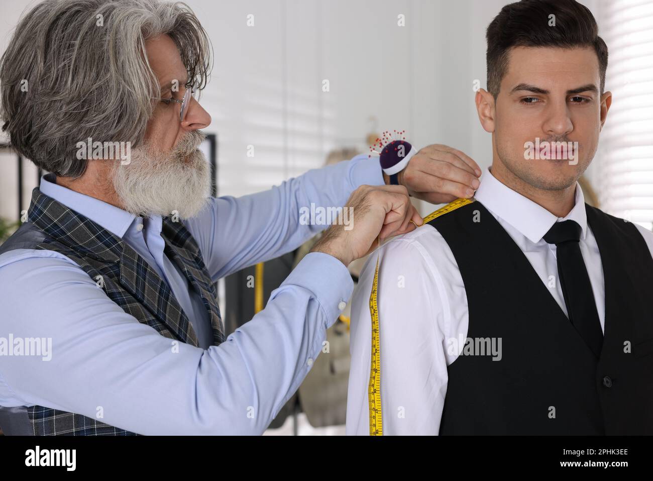 Professional tailor measuring shoulder seam length on client's vest in ...