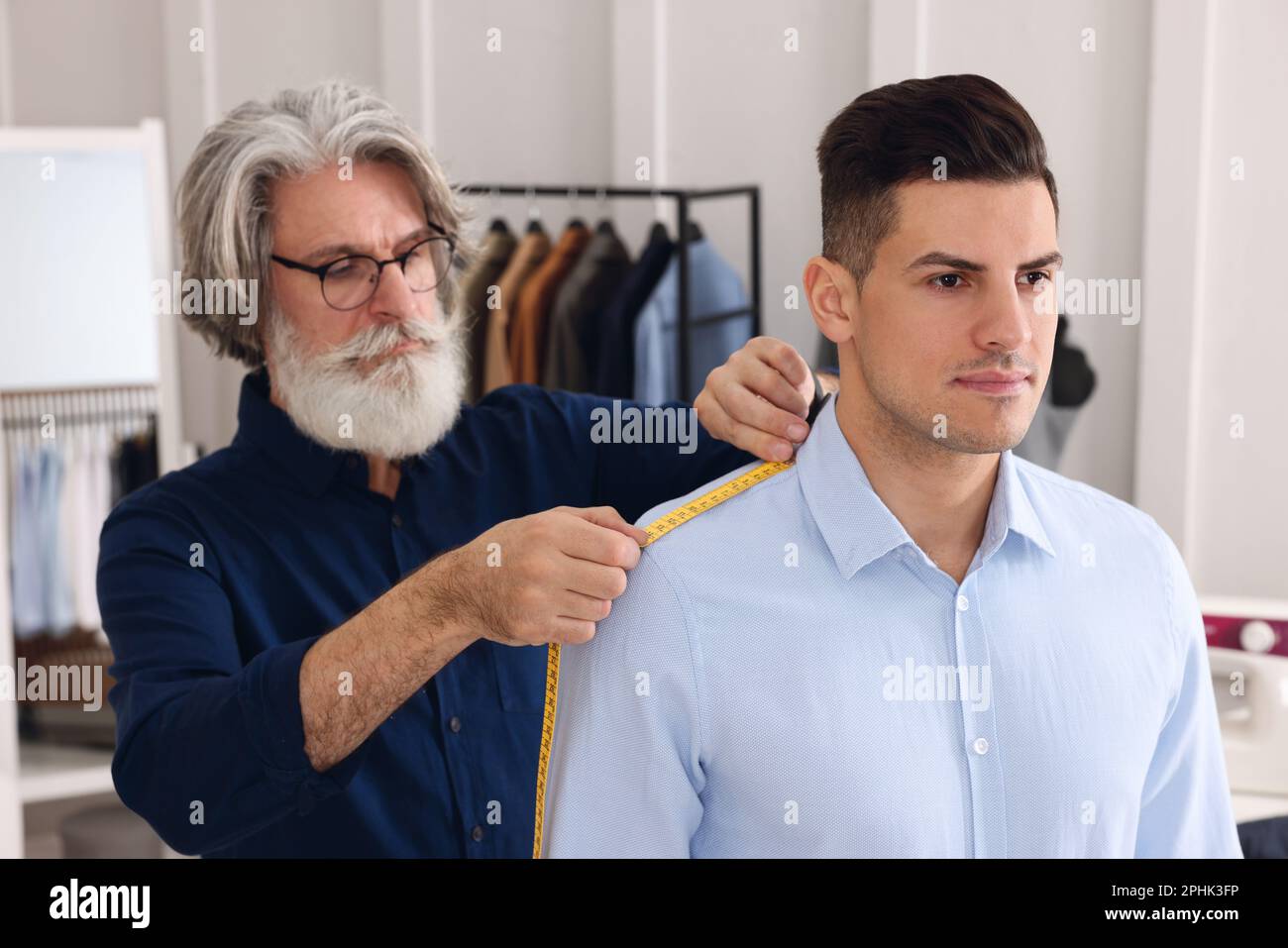 Professional tailor measuring shoulder seam length on client's shirt in ...