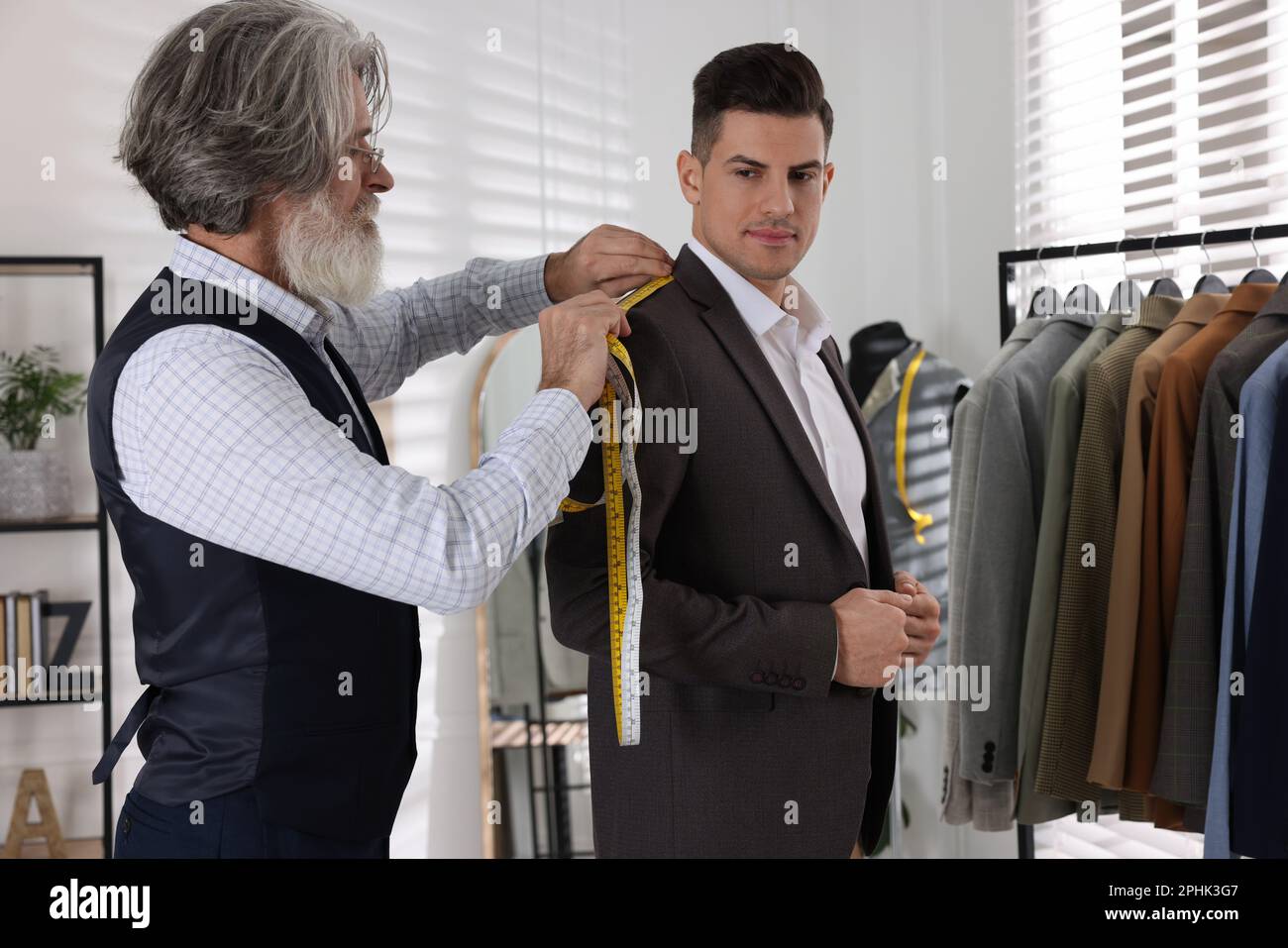 Professional tailor measuring shoulder seam length on client's jacket ...
