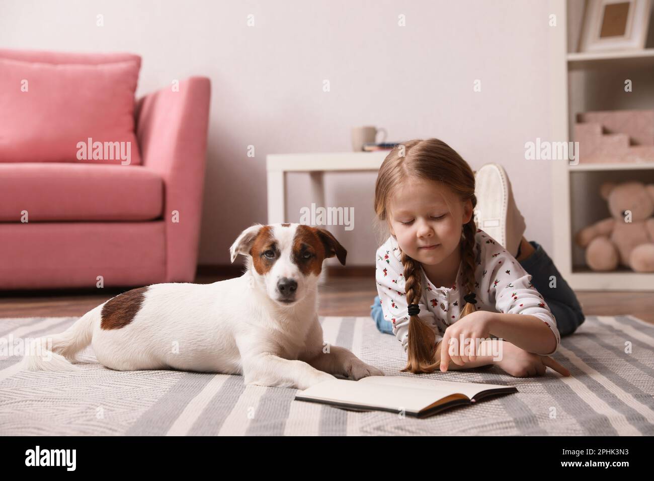 Cute little girl with her dog reading book on carpet at home. Childhood ...