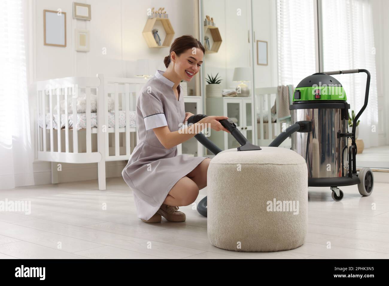 Professional chambermaid vacuuming pouf in nursery. Cleaning service ...