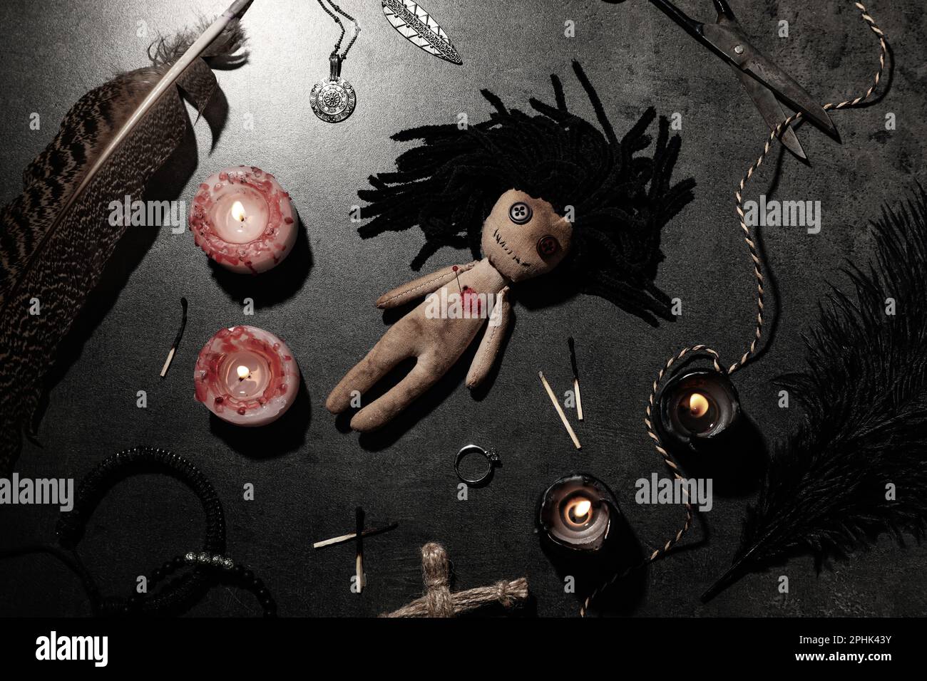 Female voodoo doll with pin in heart and ceremonial items on grey table ...