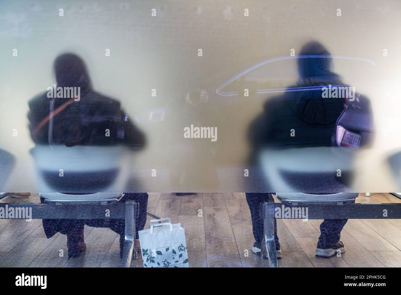 Two people seated in a waiting room, seen through translucent glass ...