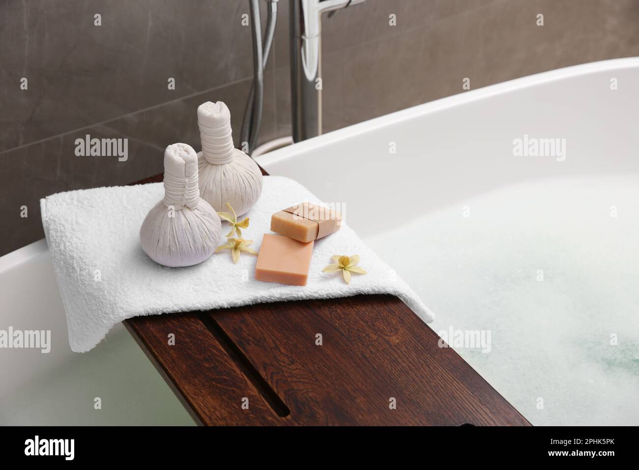 Wooden bath tray with herbal massage bags and bathroom amenities on tub ...
