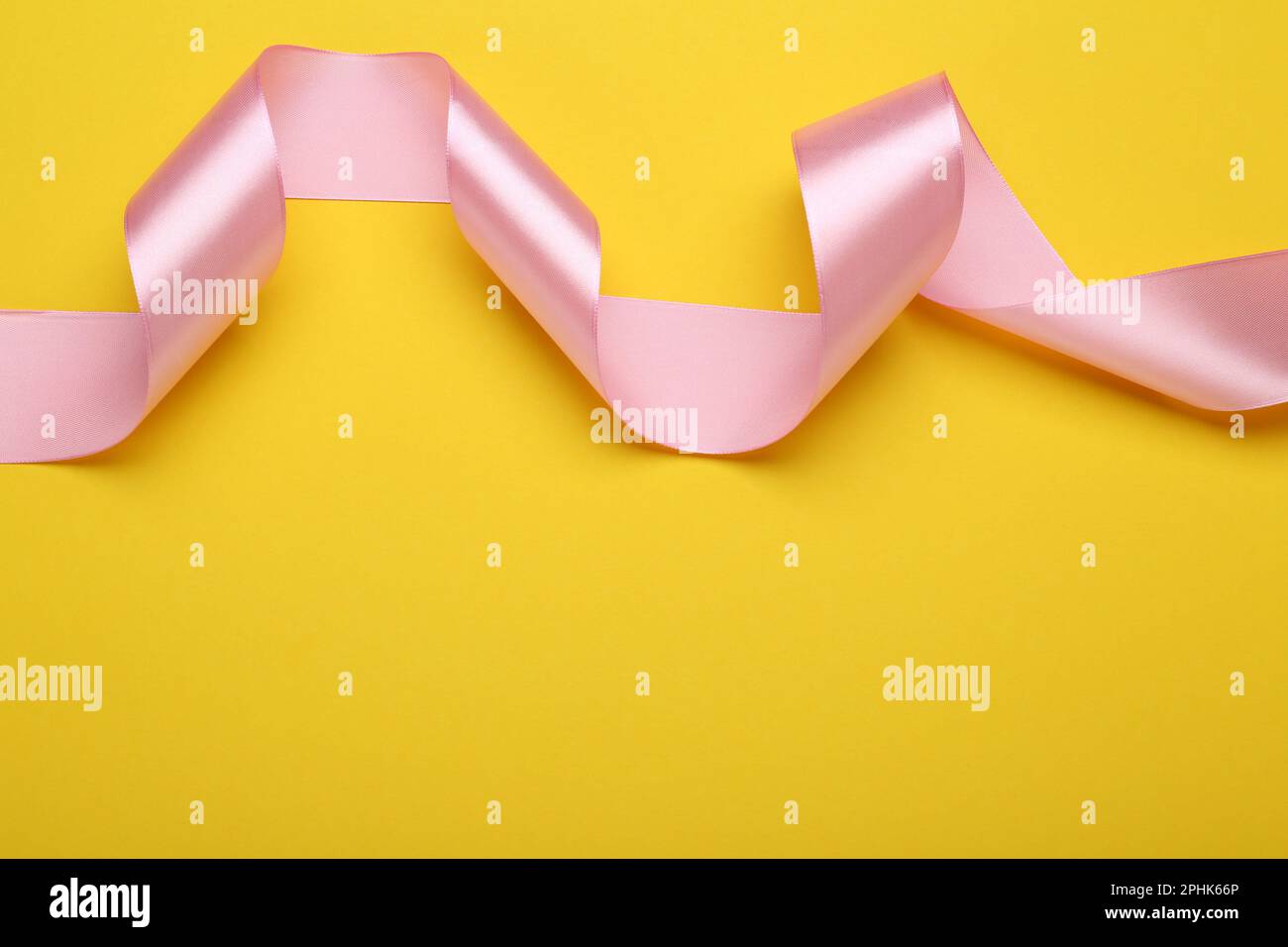 Beautiful pink ribbon on yellow background, top view. Space for text ...
