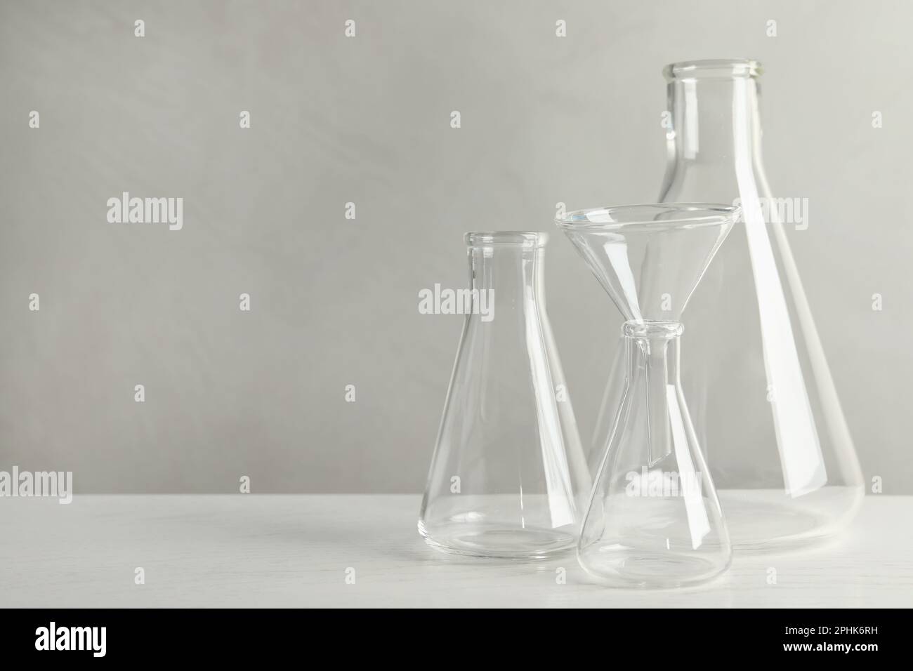 Set of laboratory glassware on white table against grey background ...