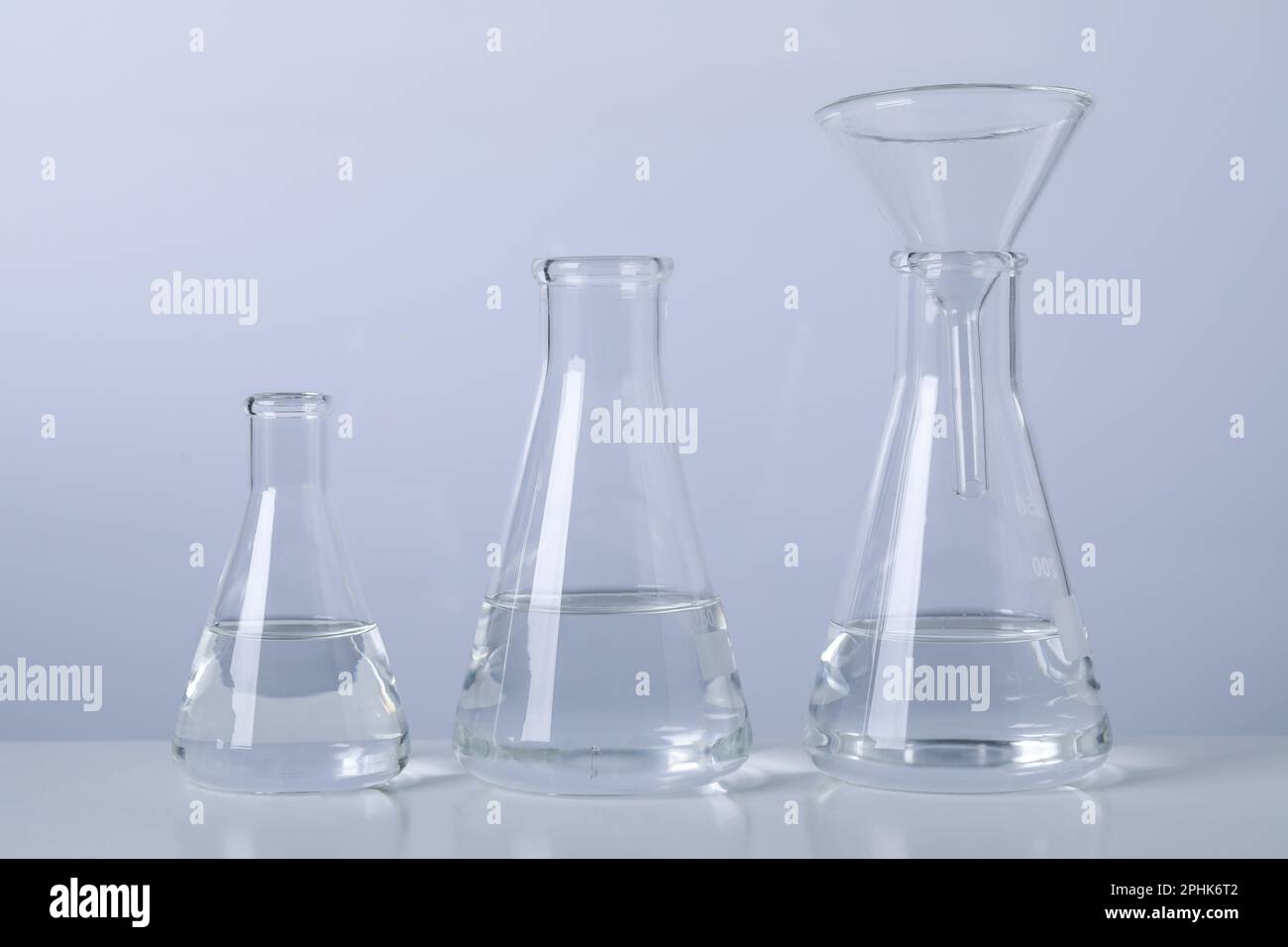 Conical flasks with transparent liquid and funnel on table against ...