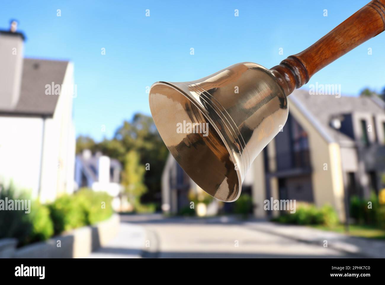 Golden school bell with wooden handle and blurred view of street on ...