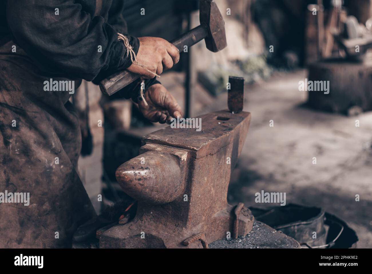 Blacksmith process metal with hammer on anvil in forge. Farrier in dirty clothes strike iron in ...
