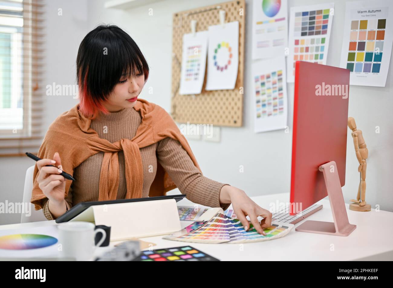 Attractive young Asian female web graphic designer focusing on her project, choosing color from ...