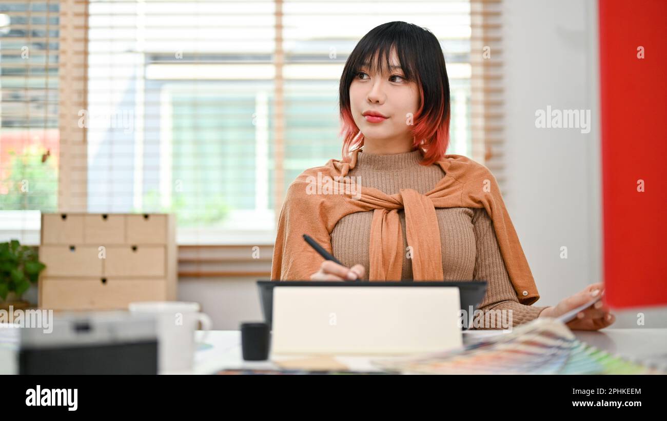 Thoughtful and inspired young Asian female graphic designer sketching a ...