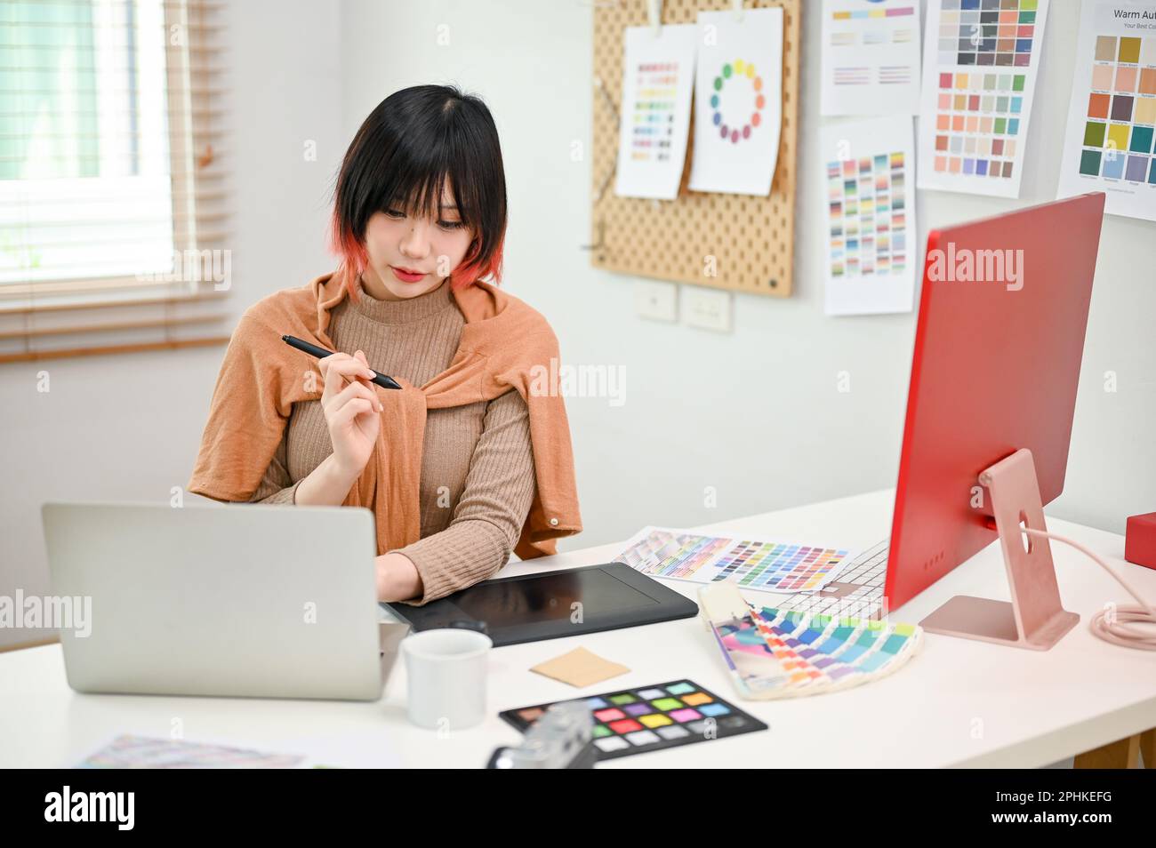 Charming young Asian female graphic designer using laptop, focusing on ...