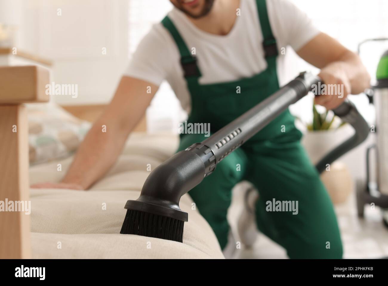 Professional janitor vacuuming sofa in living room, focus on nozzle ...