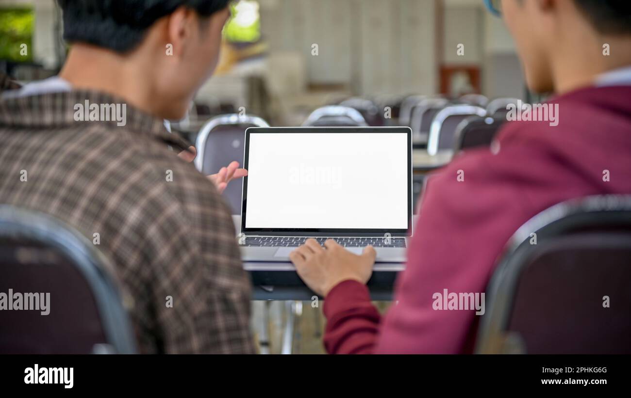 Back view, Two young Asian male college students are discussing, using laptop and working on ...