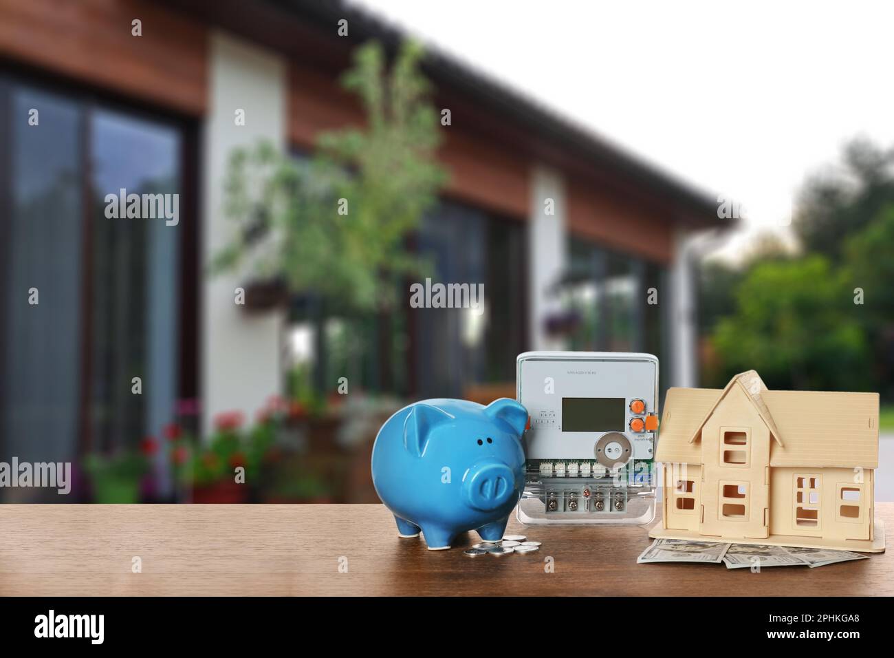 Electricity meter, house model and piggy bank on wooden table against ...