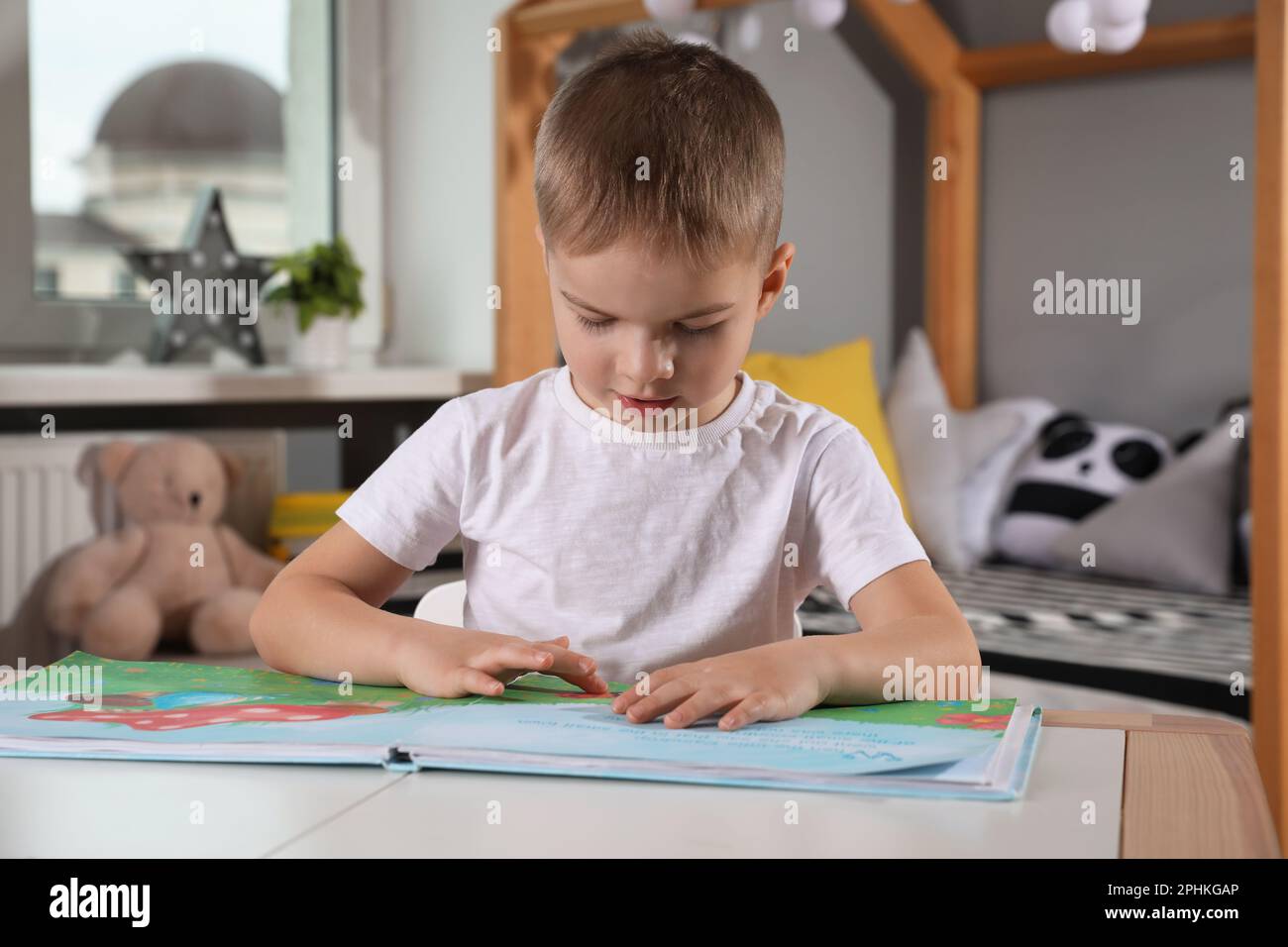 Cute little boy reading book at table in room Stock Photo - Alamy