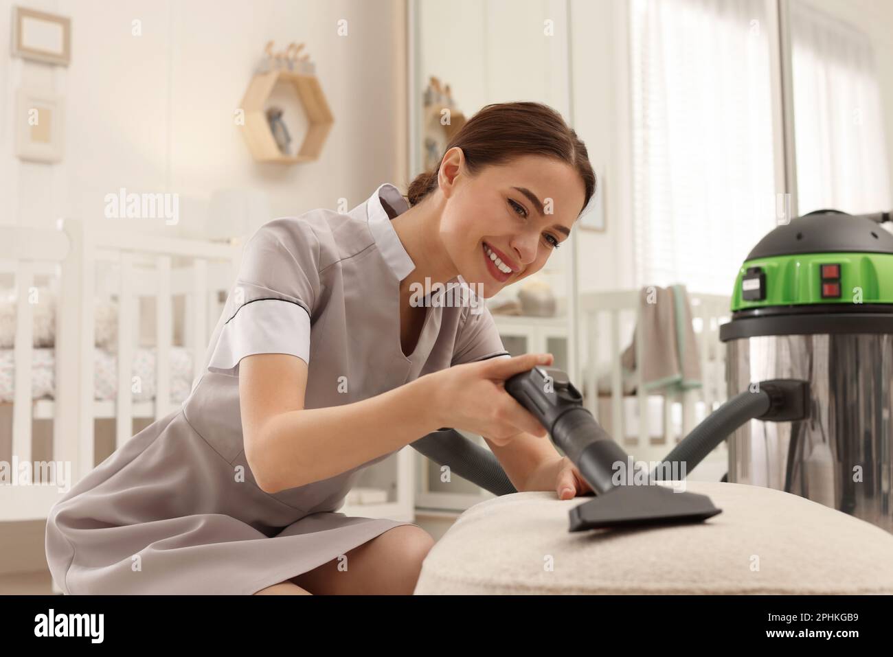 Professional chambermaid vacuuming pouf in nursery. Cleaning service ...
