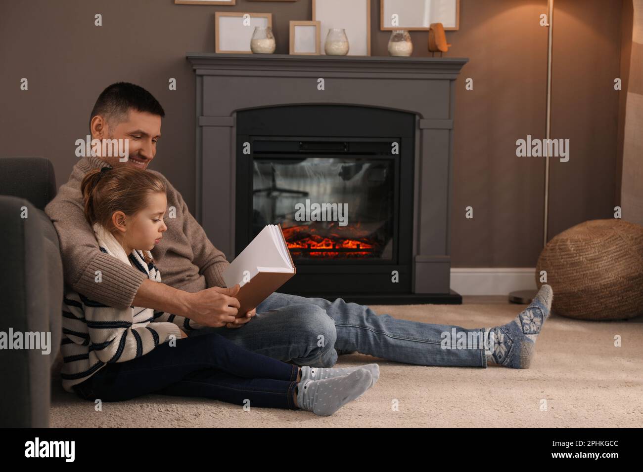 Happy father and daughter reading book together on floor near fireplace ...