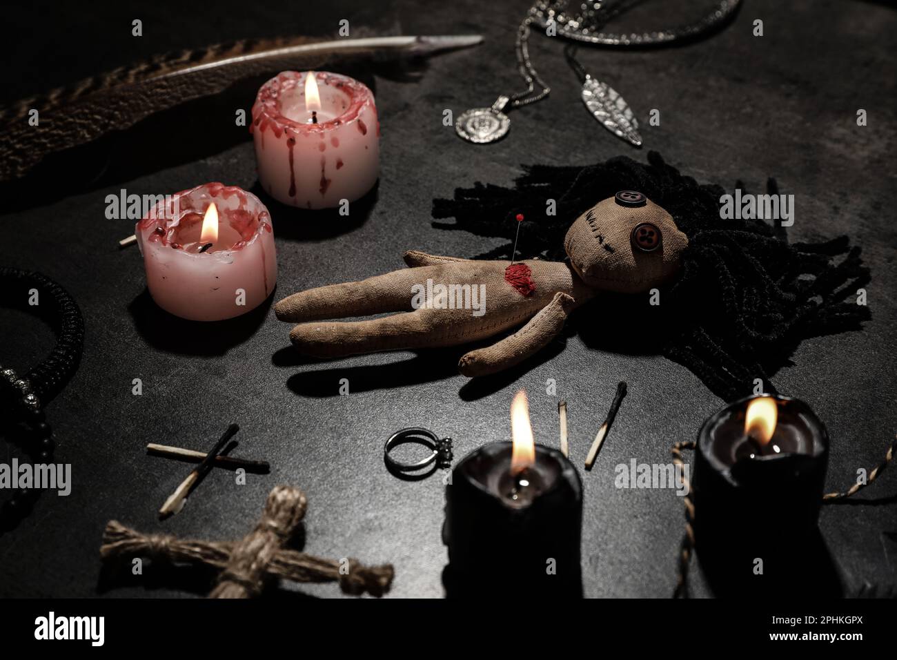 Female voodoo doll with pin in heart and ceremonial items on grey table ...