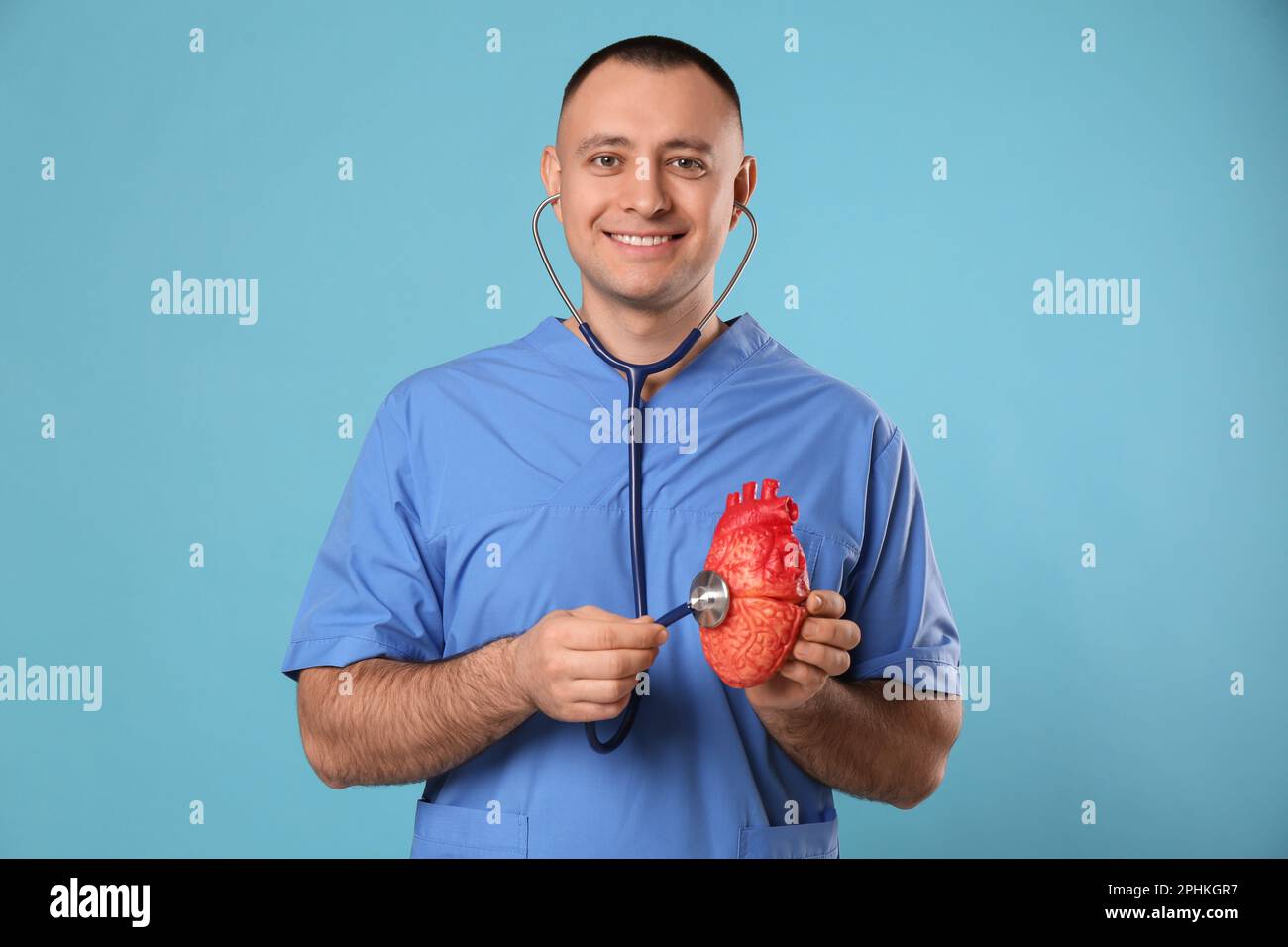 Doctor with stethoscope and model of heart on light blue background ...