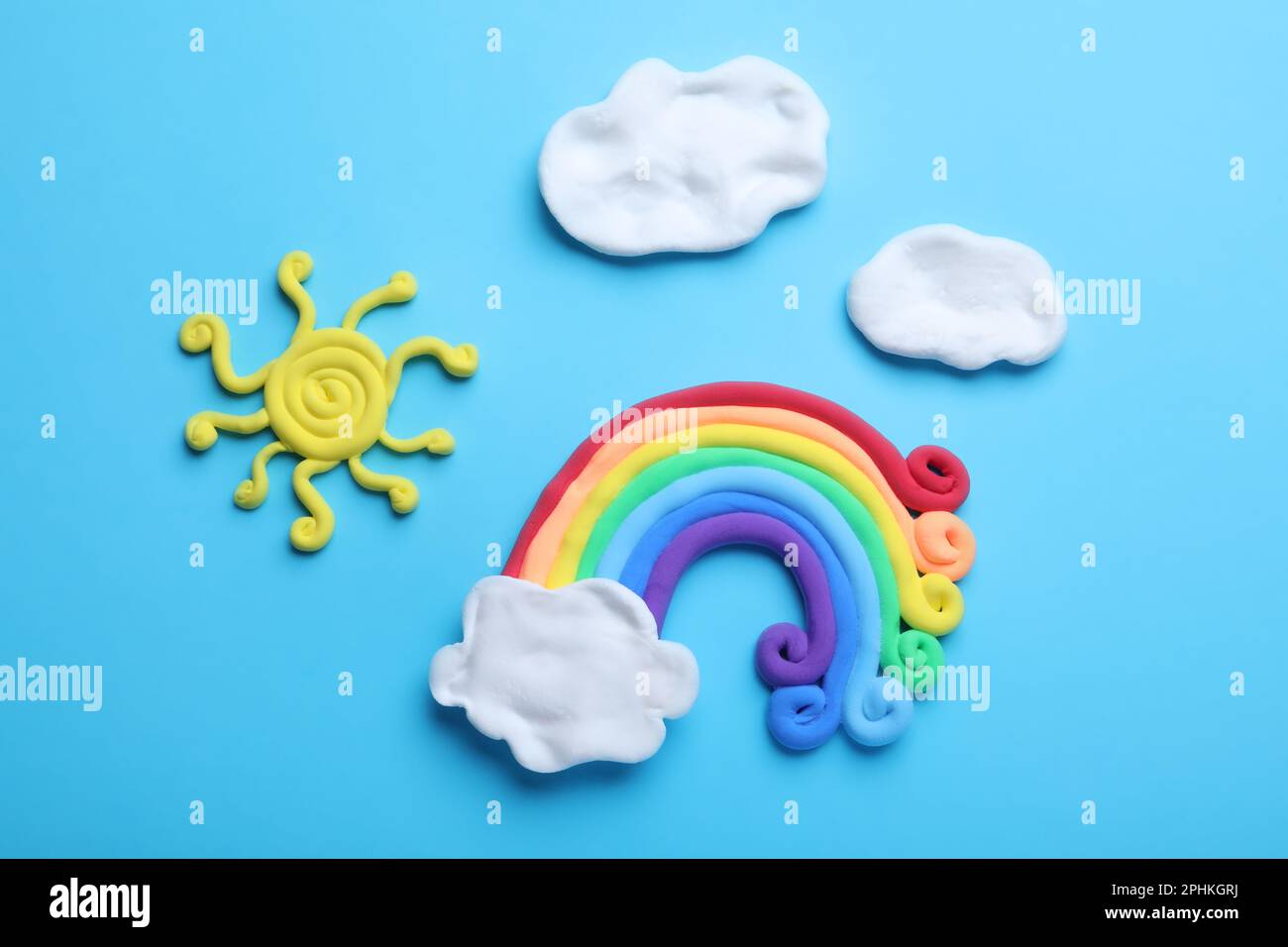 Rainbow, sun and clouds made from play dough on light blue background ...